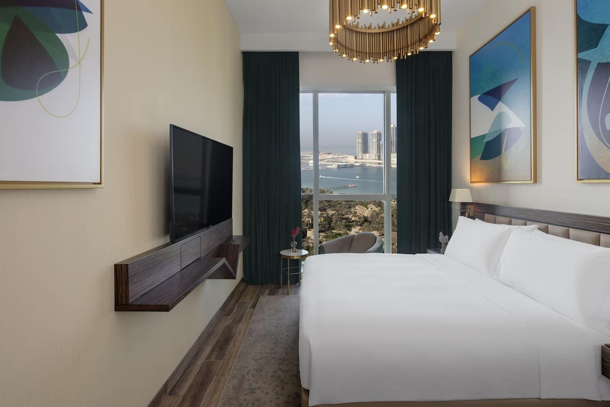 Quarto de hotel com uma cama grande, televisão de tela plana na parede, vista para a cidade através da janela e um lustre.