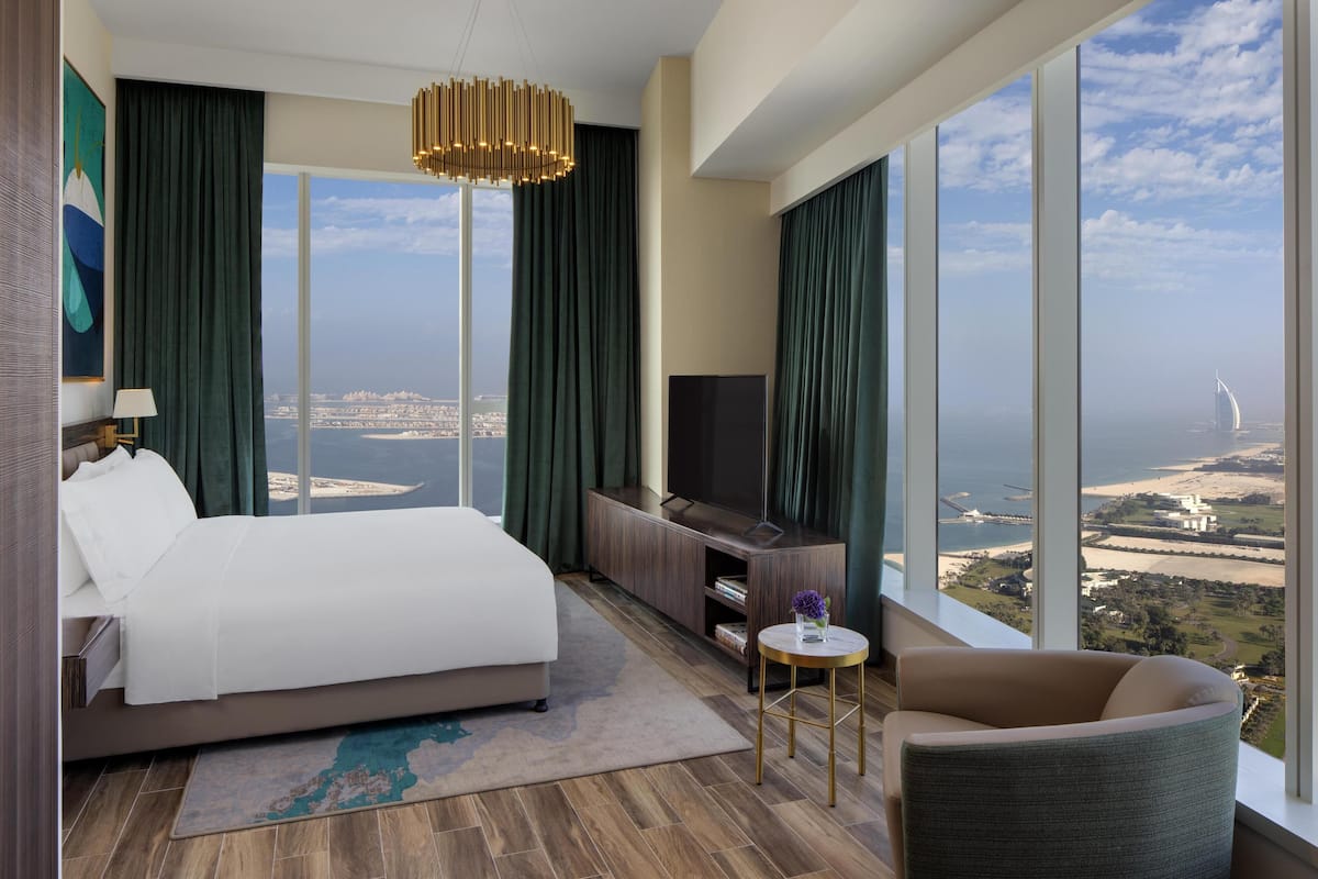 Quarto de hotel moderno com uma cama grande, televisão, mesinha e vista para a costa.