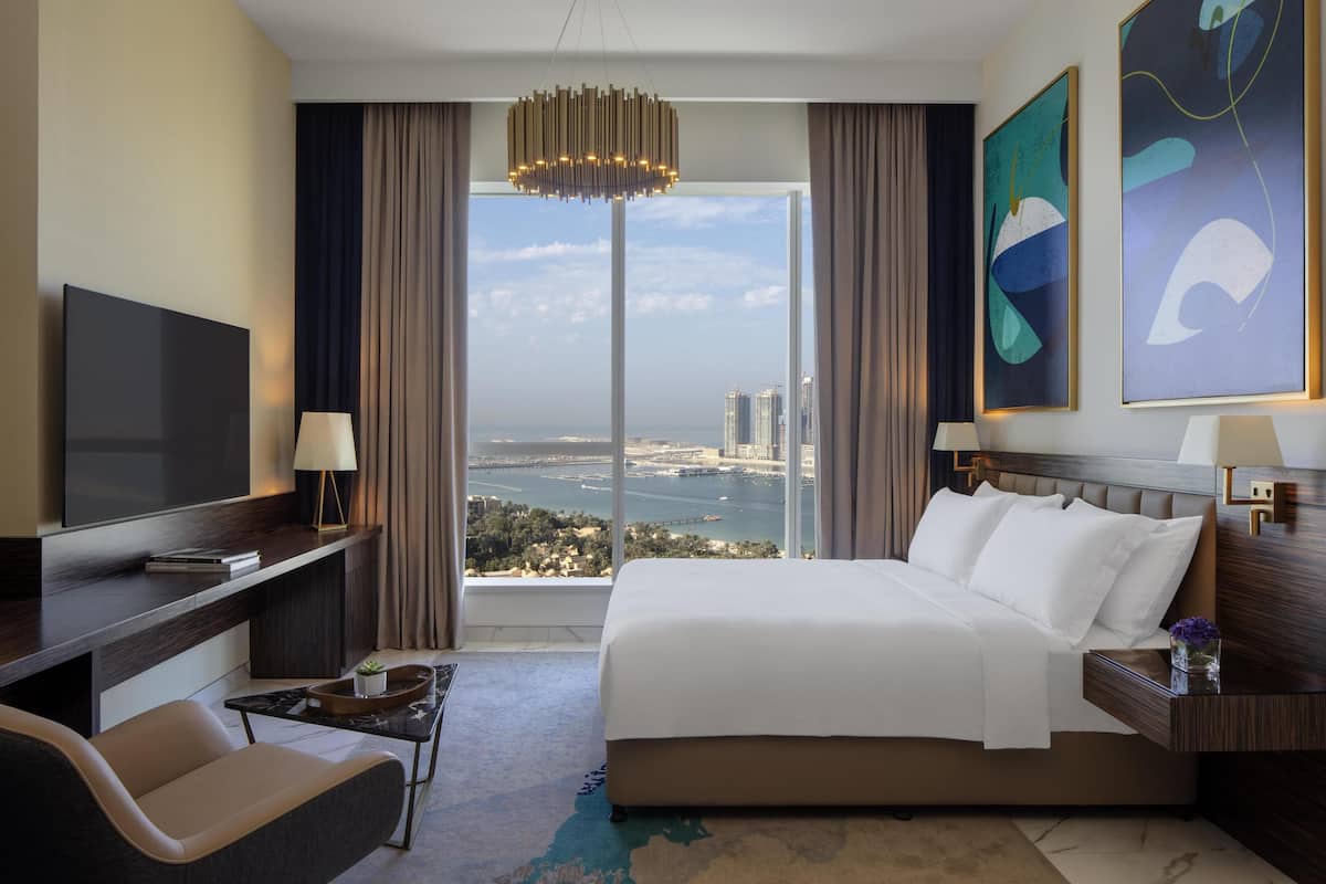 Quarto de hotel com uma cama grande, televisão, escrivaninha e vista para a cidade.