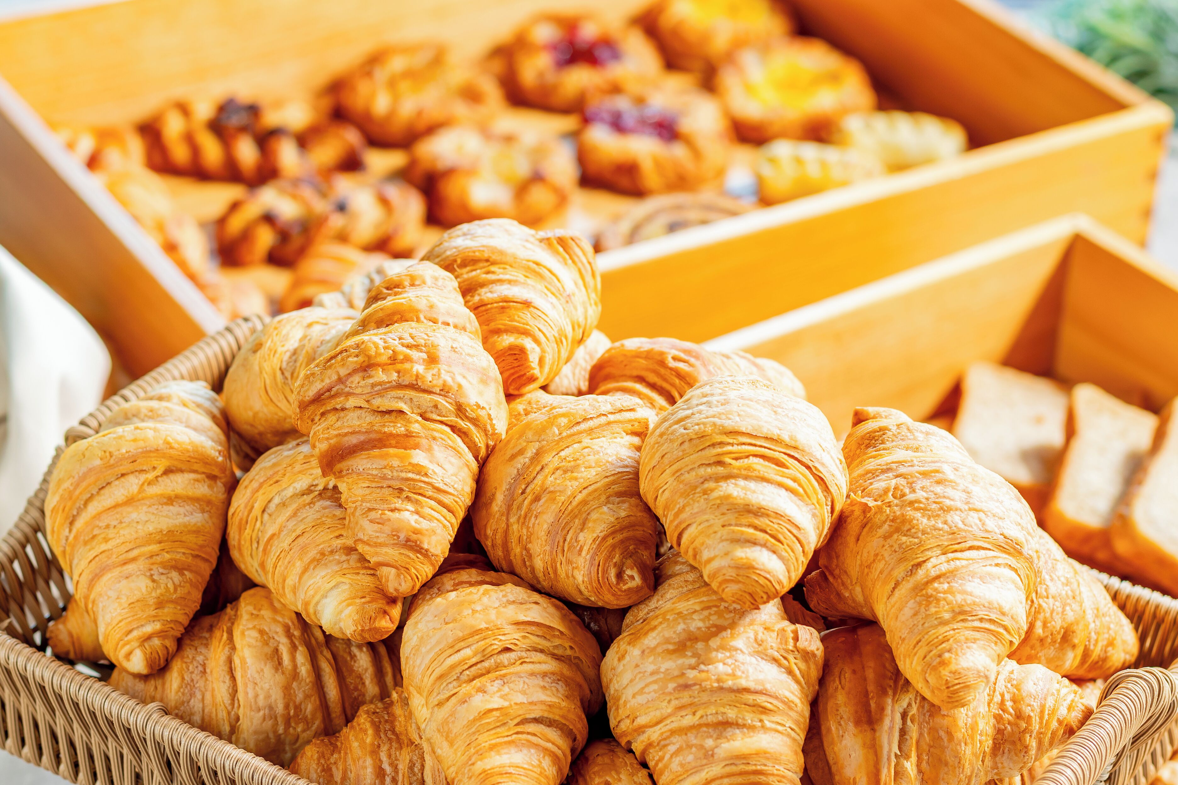Uma cesta com croissants e uma caixa de doces variados.