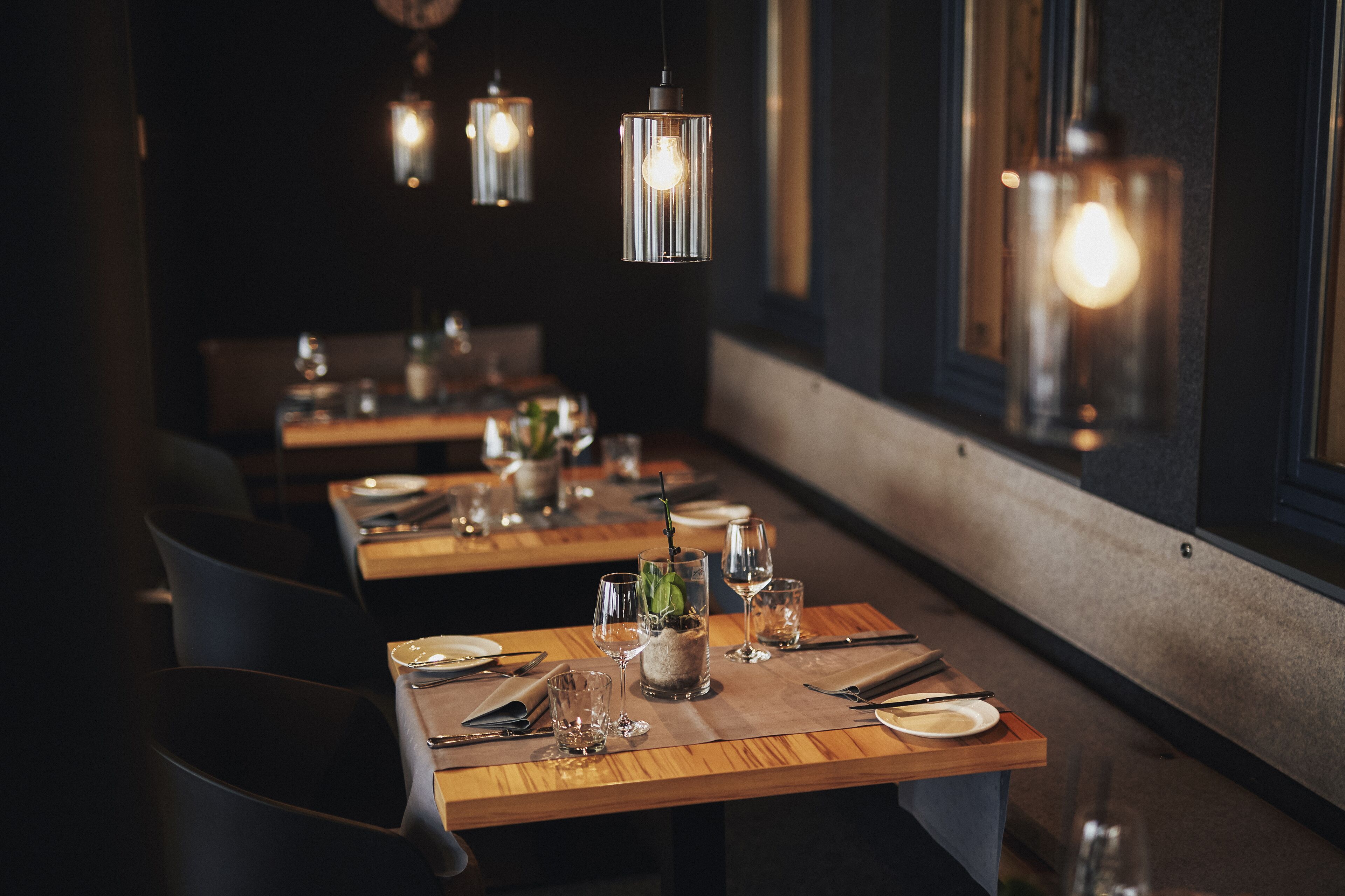 Restaurante com mesas de madeira preparadas para refeições, com copos de vidro transparentes e um centro de mesa.