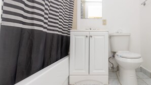 Um banheiro com vaso sanitário branco, armário branco e cortina de chuveiro listrada em preto e branco.
