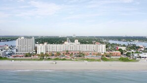 Um hotel grande com vários edifícios, uma praia ao primeiro plano e uma marina ao fundo.