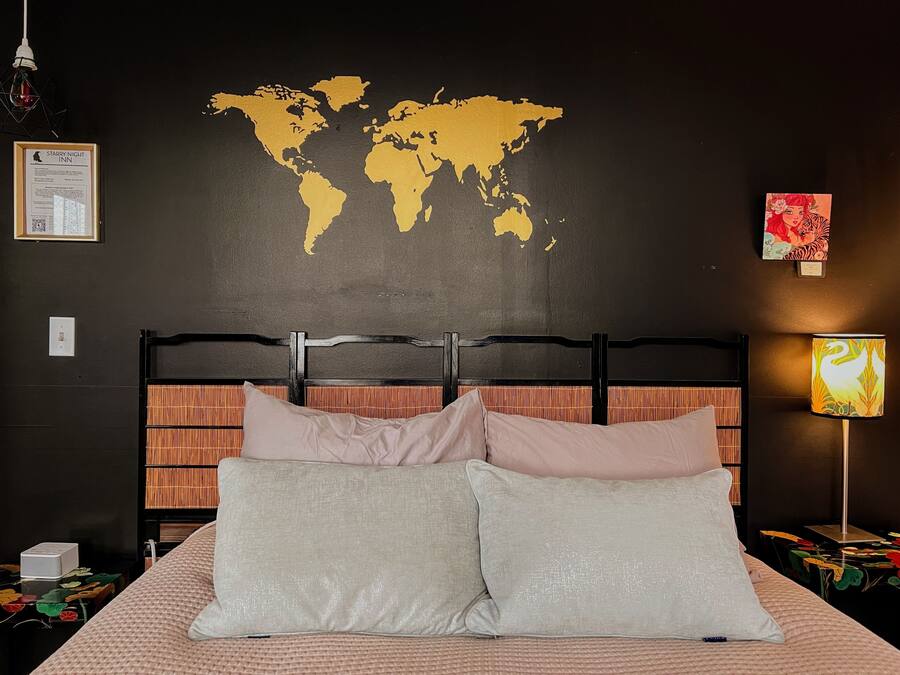 Quarto de hotel com cama, almofadas, um mapa-múndi na parede, um certificado emoldurado e uma luminária.
