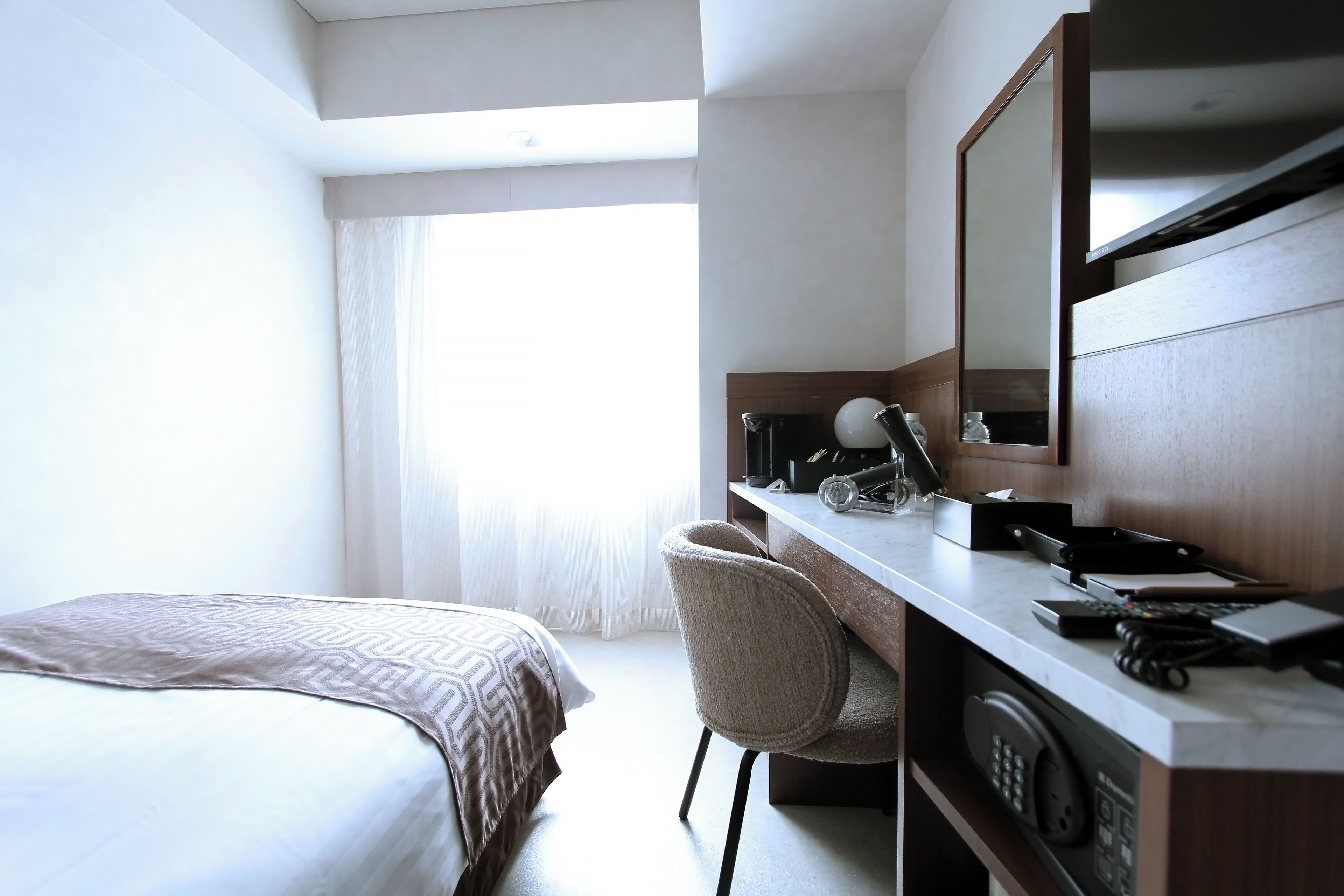 Quarto de hotel com cama, mesa com cadeira, telefone e espelho.