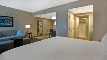Quarto de hotel com uma cama grande, um sofá, uma escrivaninha e um espelho.