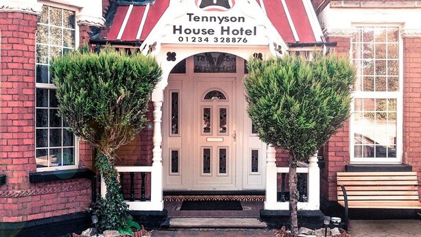 Entrada do Hotel Tennyson, com fachada tradicional, toldo listrado em vermelho e branco e duas árvores simétricas na frente.