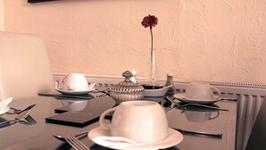 Mesa de jantar posta com pratos brancos, uma vela e um vaso com uma flor vermelha.