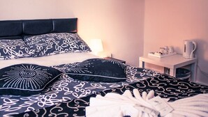 Cama bem arrumada com roupa de cama estampada, mesa de cabeceira com chaleira e luminária pendente.