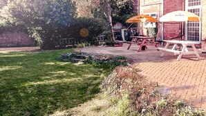 Um pátio com um edifício de tijolos, uma mesa de madeira e um guarda-sol.
