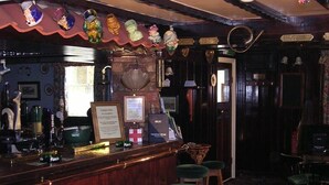 Uma área de bar com balcão de madeira, banquetas e diversos itens de bar.