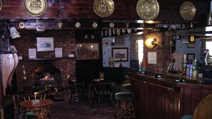 Uma área de bar com móveis de madeira, uma lareira e diversas quadros nas paredes.