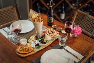 Uma mesa de jantar posta com diversas comidas, incluindo um tábua de frios, uma garrafa de vinho e copos.