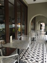 Um espaço de refeições interno com mesas e cadeiras, um chão estampado e vista para a rua através de uma porta de vidro.