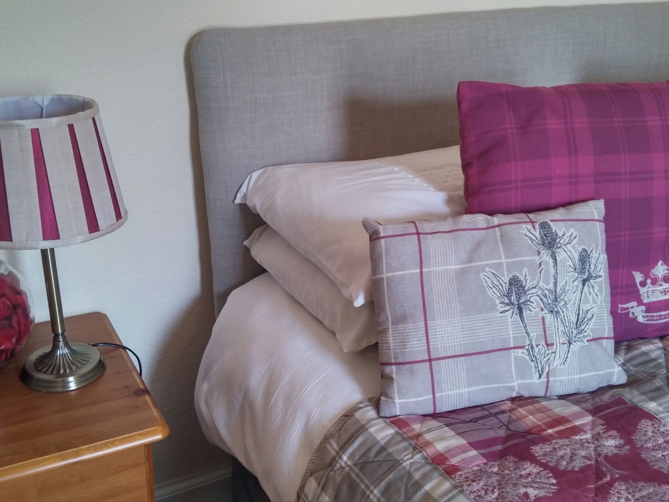 Cama bem arrumada com várias almofadas, abajur e uma pequena mesa de cabeceira de madeira.
