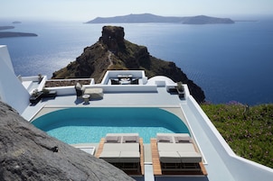 Piscina com espreguiçadeiras, vista para o mar e paisagem rochosa.
