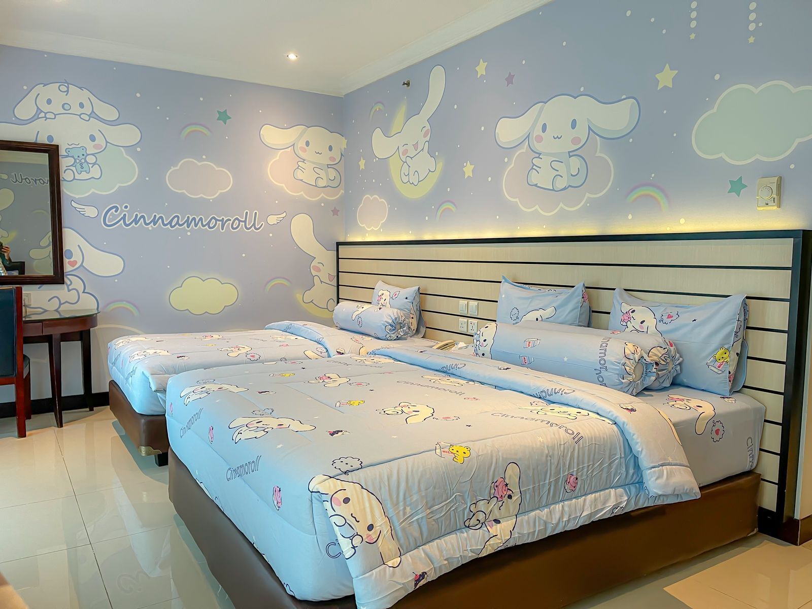 Quarto com cama decorada com tema de nuvem e coelhinho, mesa de cabeceira e espelho.