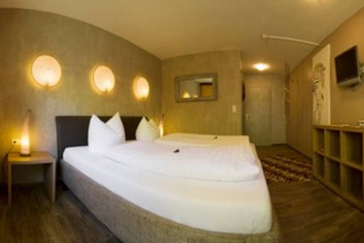 Quarto de hotel com cama grande, abajures, espelho e televisão na parede.