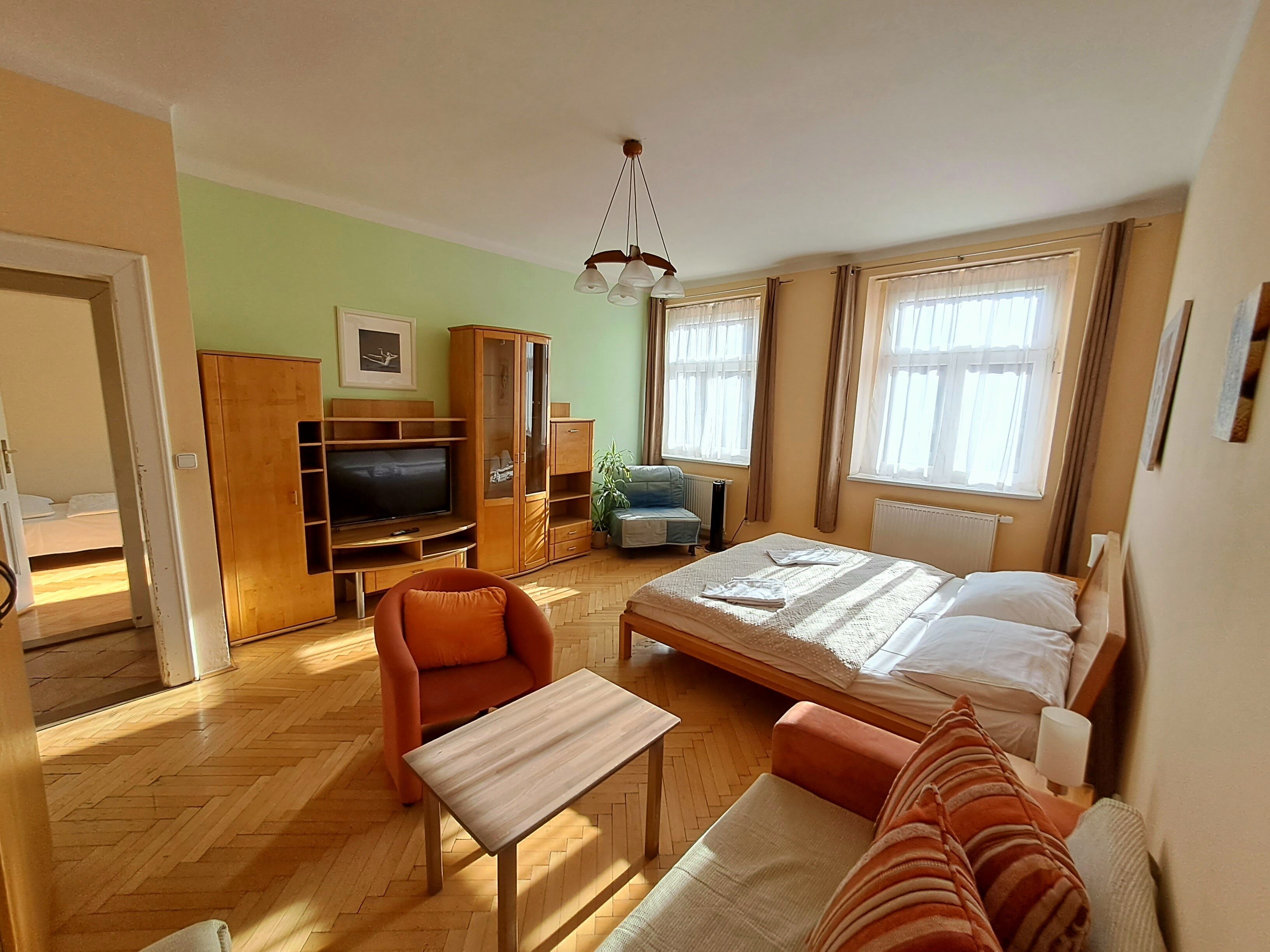 Um quarto bem iluminado, com cama, televisão, sofá e um armário de madeira.