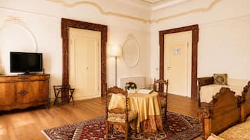 Quarto com piso de madeira, uma cama com cabeceira, escrivaninha com luminária, televisão sobre um móvel de madeira e um espelho grande na parede.
