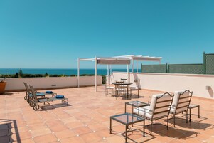 Um terraço com mobiliário externo, uma pérgula e vista para o mar.