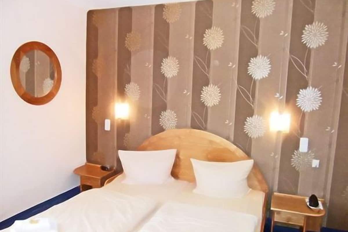 Quarto de hotel com uma cama grande, duas mesas de cabeceira, um espelho redondo e luminárias fixadas na parede.