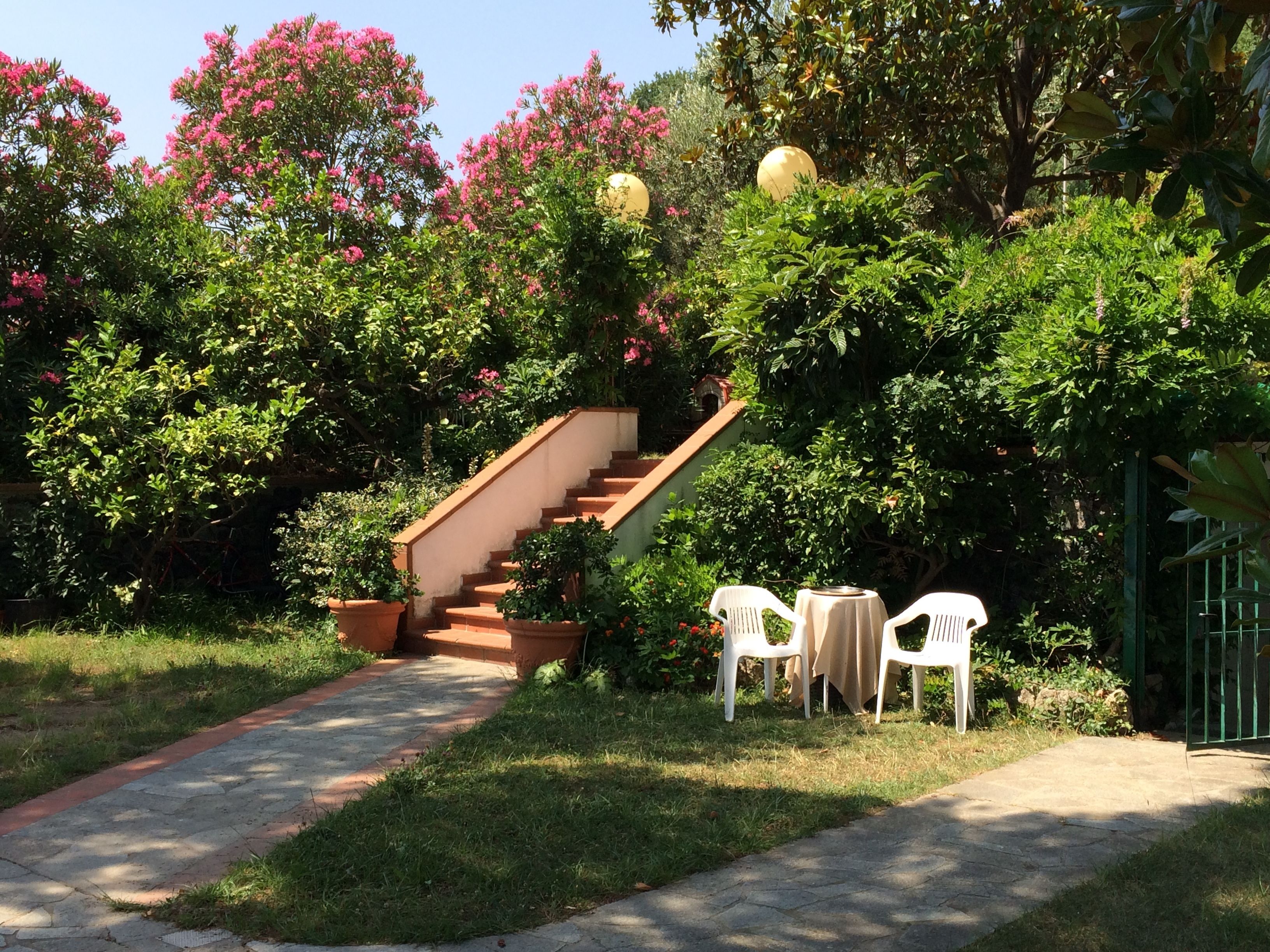 Um jardim com uma escadaria de pedra que leva a um espaço de estar com duas cadeiras de plástico branco e uma mesa.