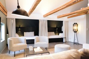 Quarto de hotel moderno com uma cama grande, duas poltronas, uma mesa de centro e um abajur.