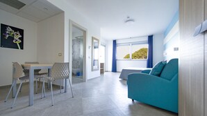 Uma sala de estar moderna com um sofá azul-turquesa, uma área de jantar com mesa e cadeiras, e uma janela grande com cortinas.