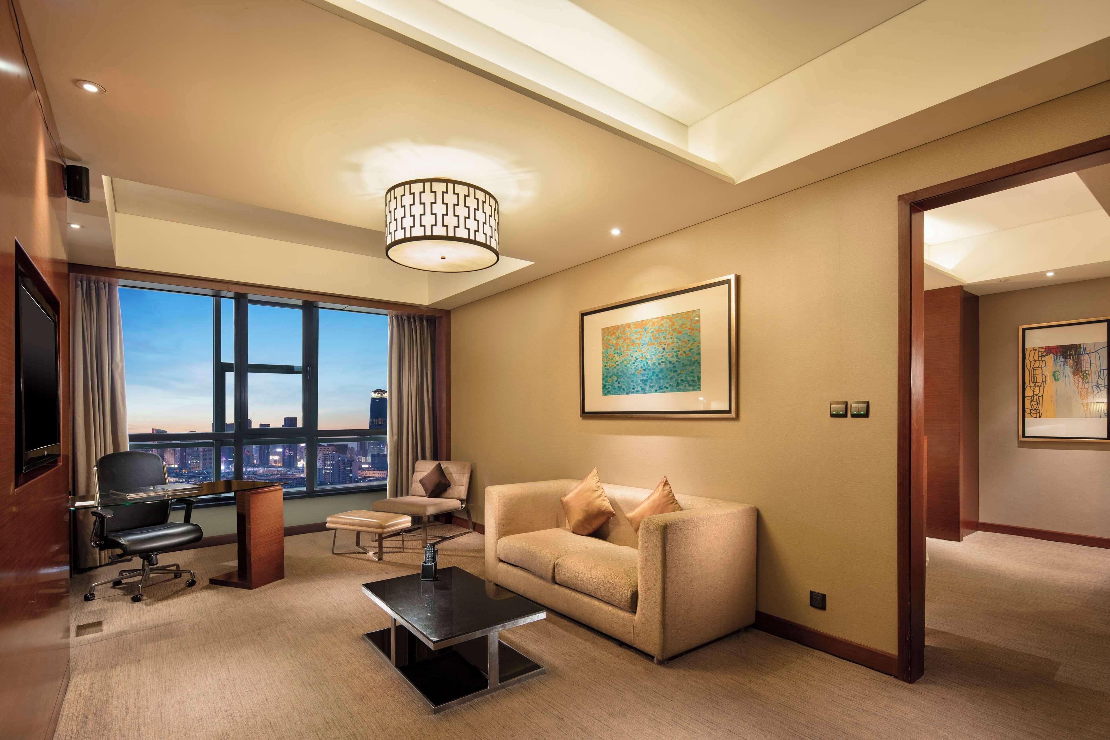 Quarto de hotel moderno com uma grande janela, um sofá, uma escrivaninha e uma mesa de centro.
