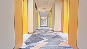 Corredor de hotel com carpete estampado, portas de ambos os lados e uma placa indicando os números dos quartos.
