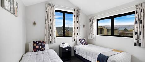 Quarto com duas camas, uma mesinha de cabeceira e janela com cortinas.