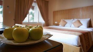 Quarto de hotel com cama, mesa de cabeceira e uma travessa de maçãs, e cortinas.