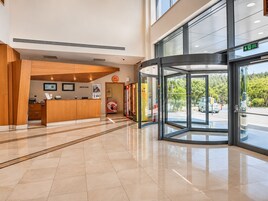 Uma área de recepção de hotel com balcão de madeira, placa indicativa e porta de vidro que dá para o exterior.