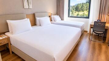 Quarto de hotel com duas camas, uma escrivaninha e vista para uma floresta pela janela.