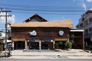 Edifício com telhado de palha, duas lojas com letreiros e um estacionamento em frente.