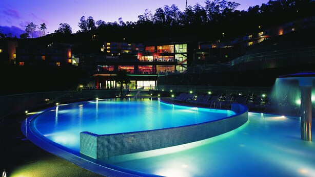Piscina ao entardecer com vista para edifícios de hotel ao fundo.