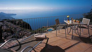 Terraço com mesa posta para o café da manhã, com vista para a costa.
