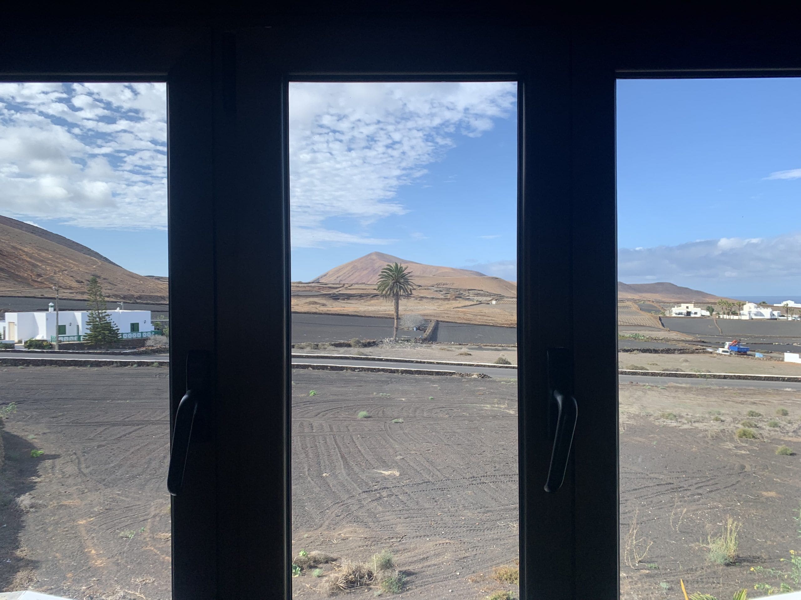 Visão pela janela de uma paisagem árida com montanha, vegetação rala e alguns edifícios.