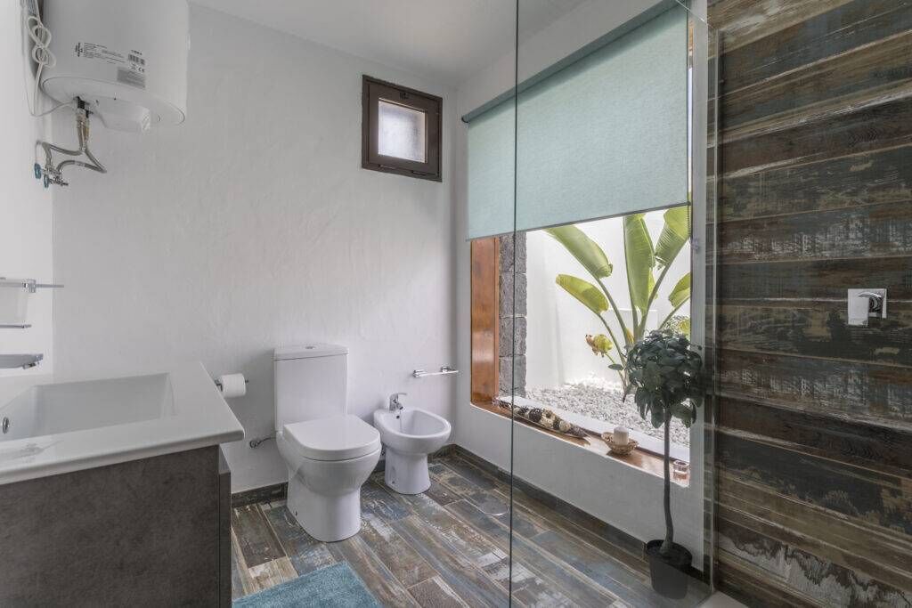 Casa de banho moderna com banheira, sanita, bidé e uma janela grande com vista para plantas.