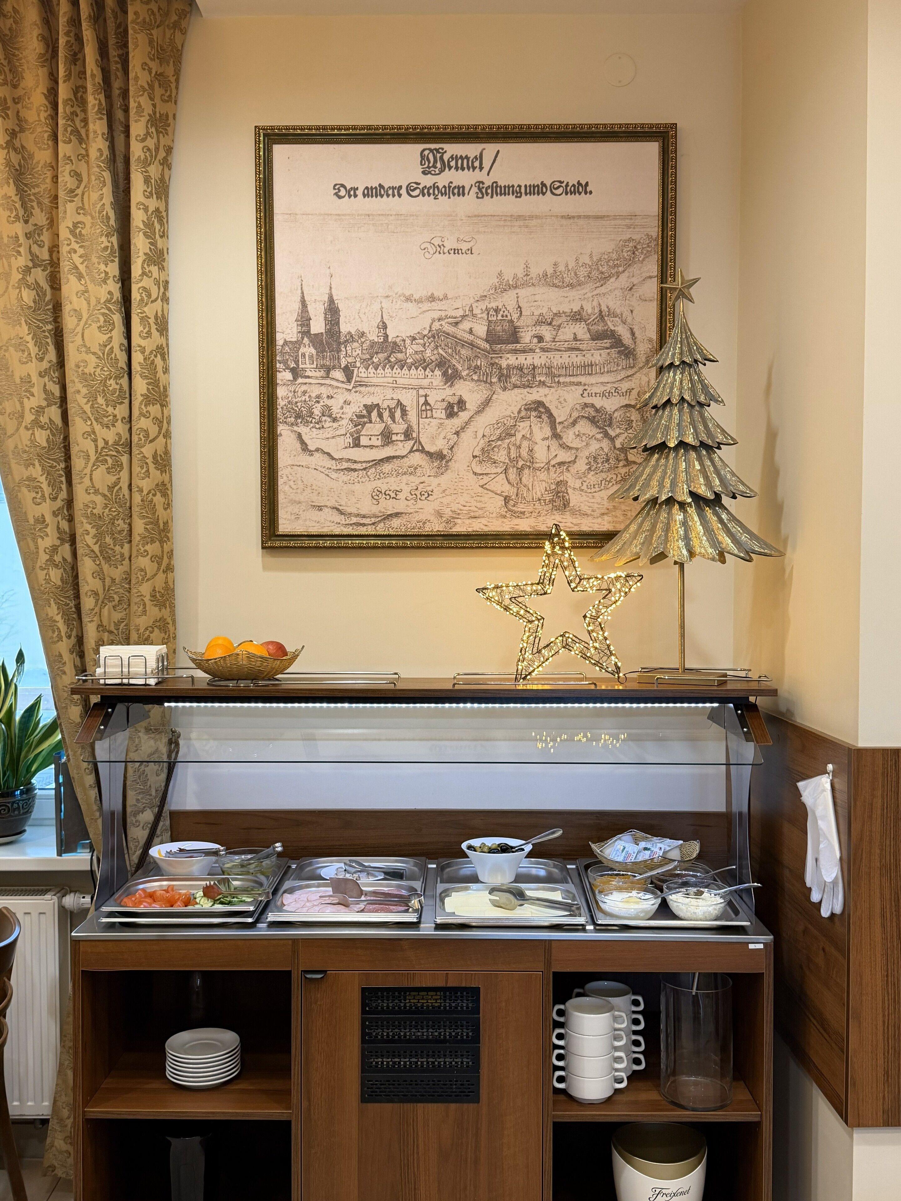 Disposição de buffet com diversos alimentos, um mapa histórico emoldurado, um pinheiro de Natal decorativo e um enfeite de estrela em um suporte.
