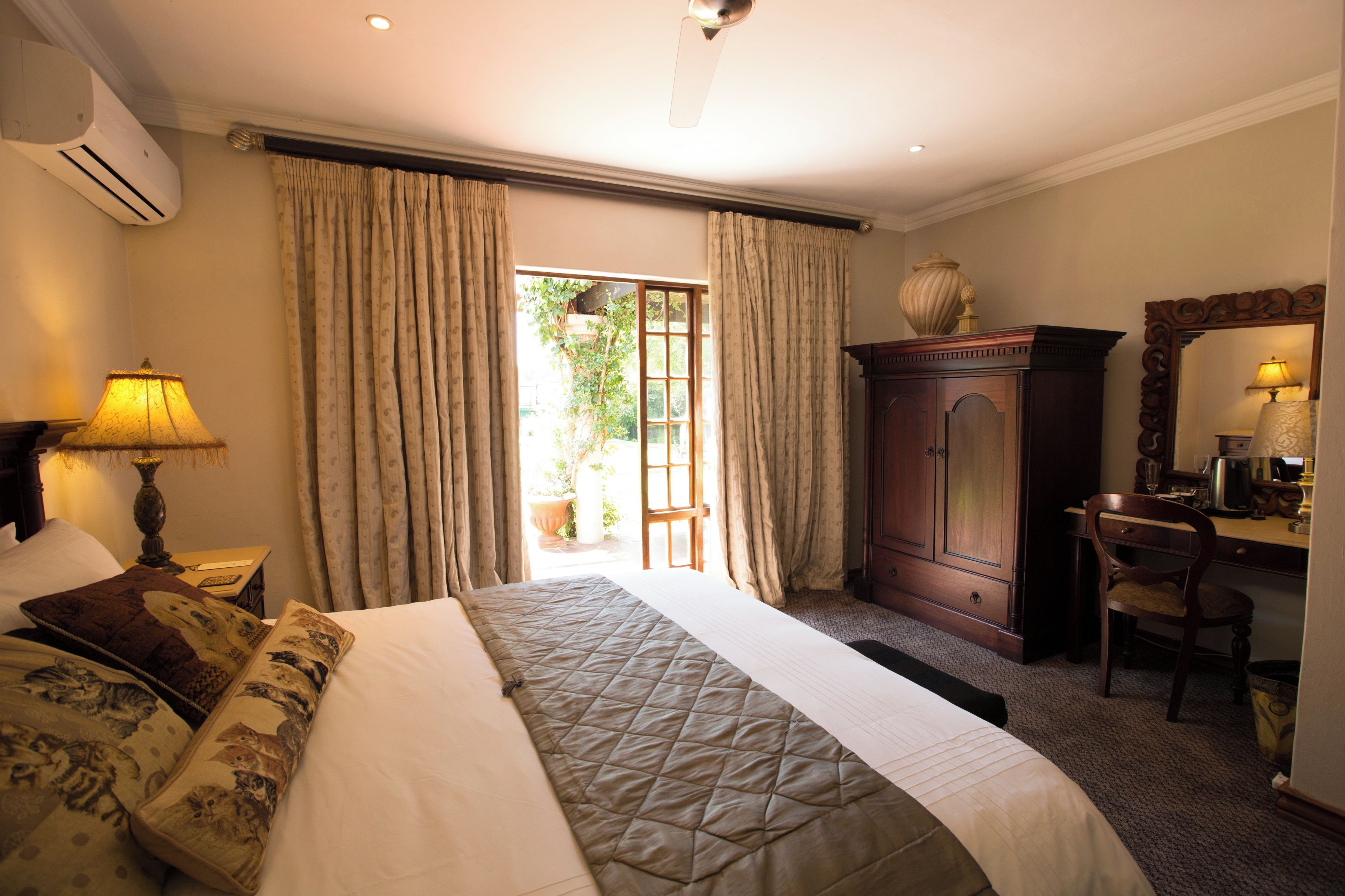 Quarto de hotel com cama, escrivaninha, cadeira, guarda-roupa e uma janela grande com cortinas.