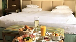 Quarto de hotel com uma cama, uma bandeja de café da manhã com croissants, um copo de suco e uma xícara de café.