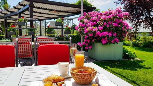 Uma área de refeições ao ar livre com uma mesa posta para o café da manhã, incluindo croissants, torradas e uma cesta de pão.