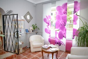 Quarto com poltrona branca, vitrine de vidro e ampla janela com vista exterior.