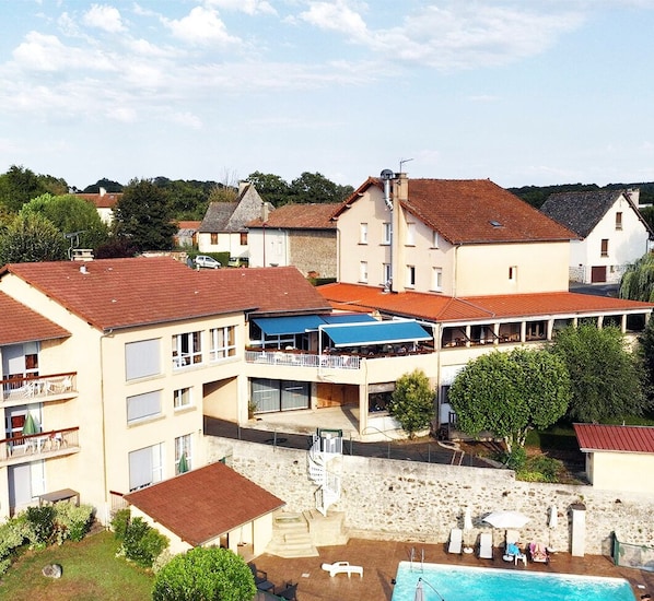 Um hotel com vários andares, piscina, área de estar externa e um alpendre coberto.
