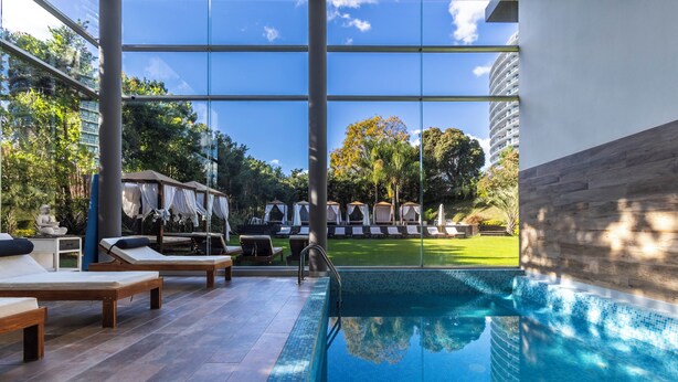 Piscina interior com espreguiçadeiras e vista para uma área gramada e árvores.