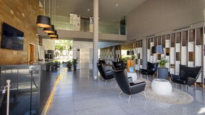 Um saguão de hotel moderno, com espaço amplo, balcão de recepção, assentos confortáveis e uma grande tela de televisão.