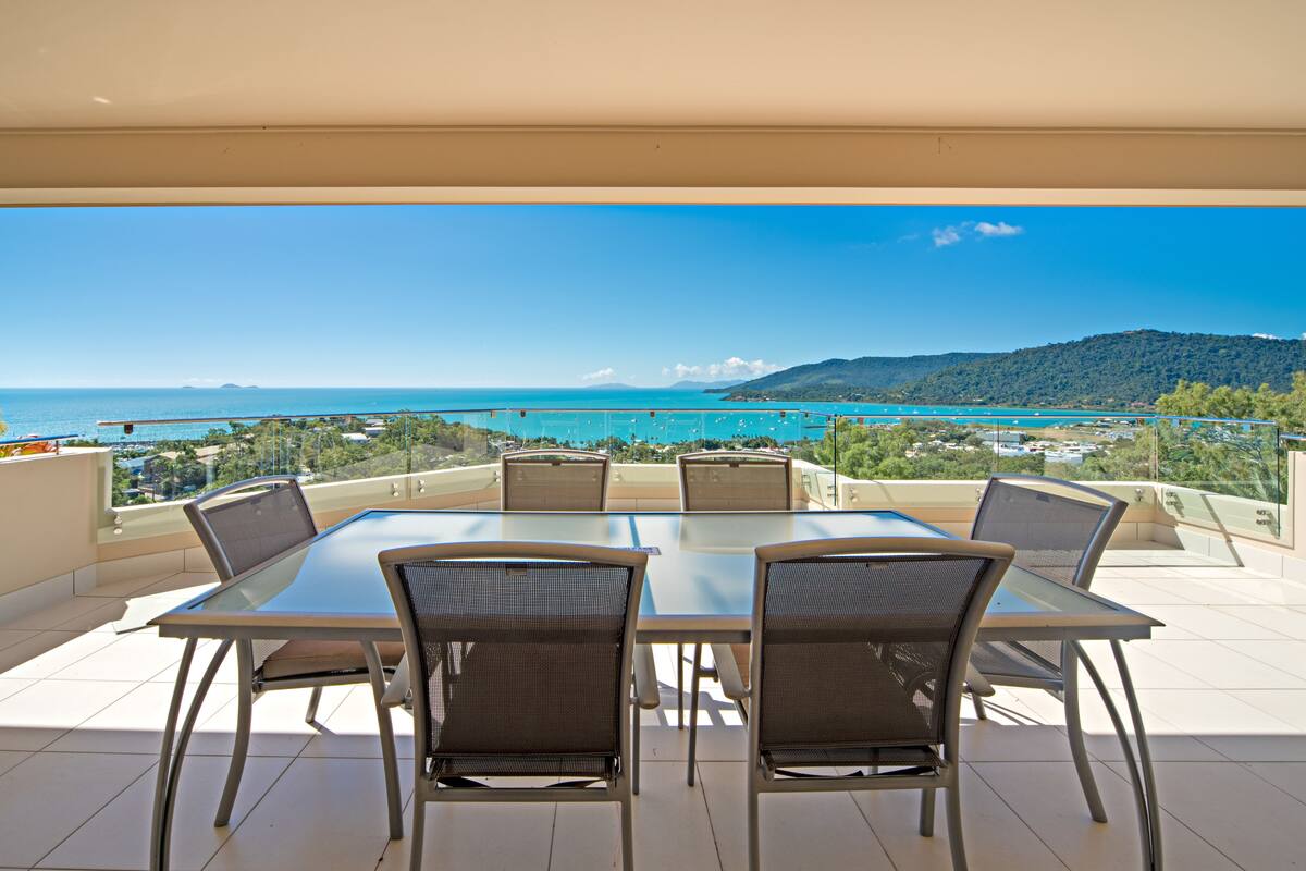 Uma área de refeições com mesa e cadeiras com vista para o mar e as montanhas.