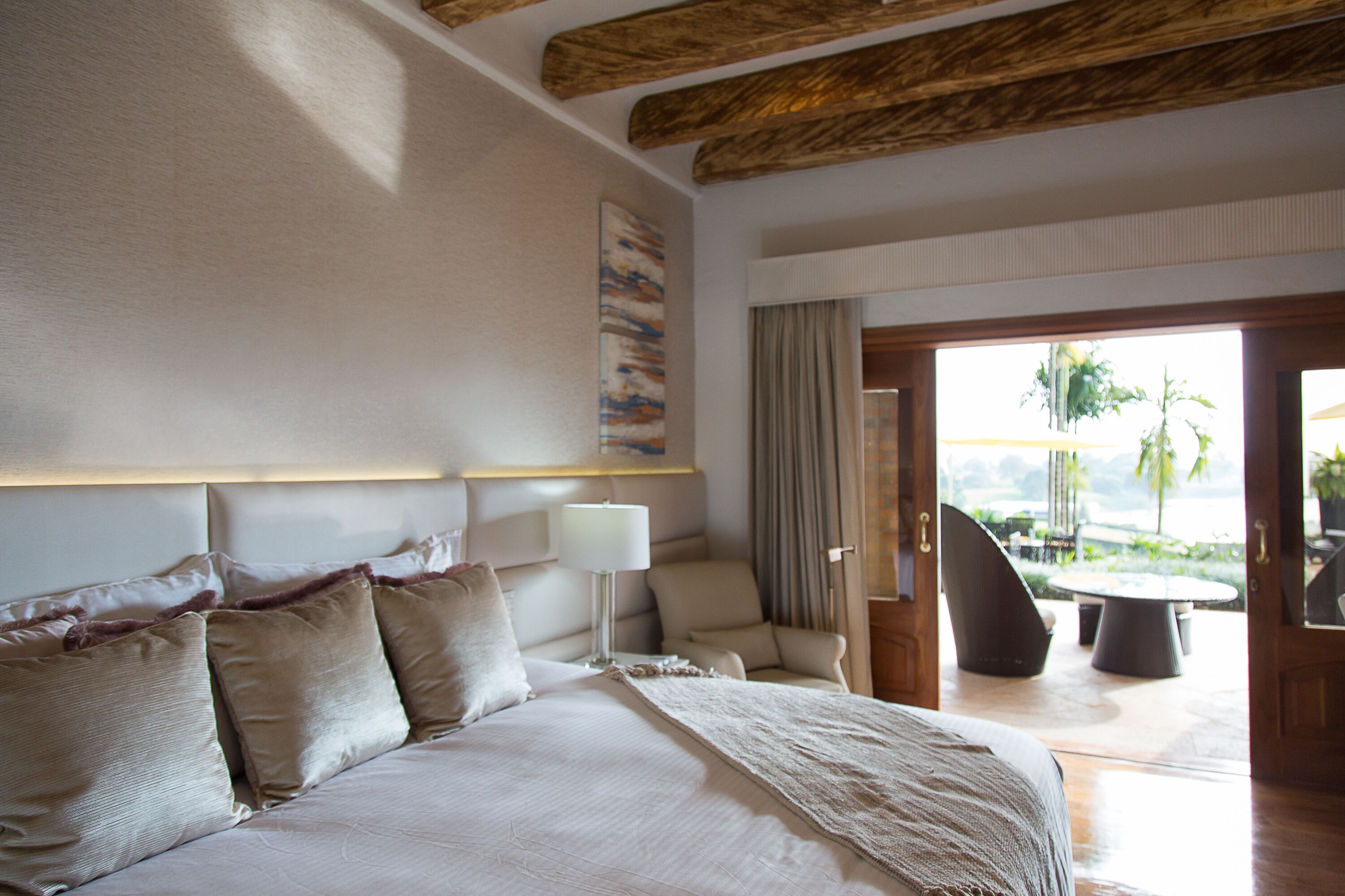 Quarto de hotel com uma cama grande, mesa de cabeceira com abajur, uma cadeira e vista para o exterior.